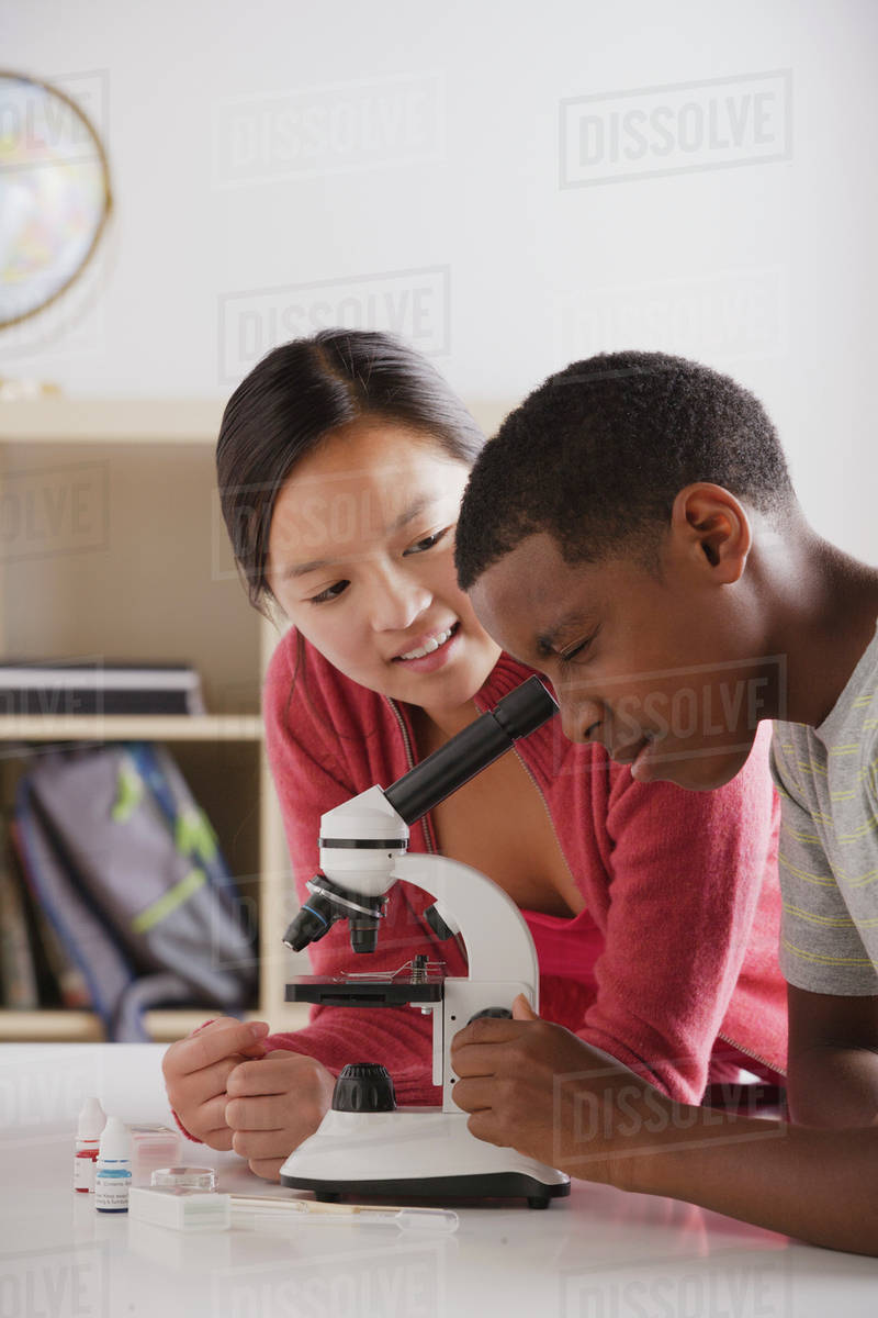 Teenage students (14-15) working with microscope - Stock Photo - Dissolve
