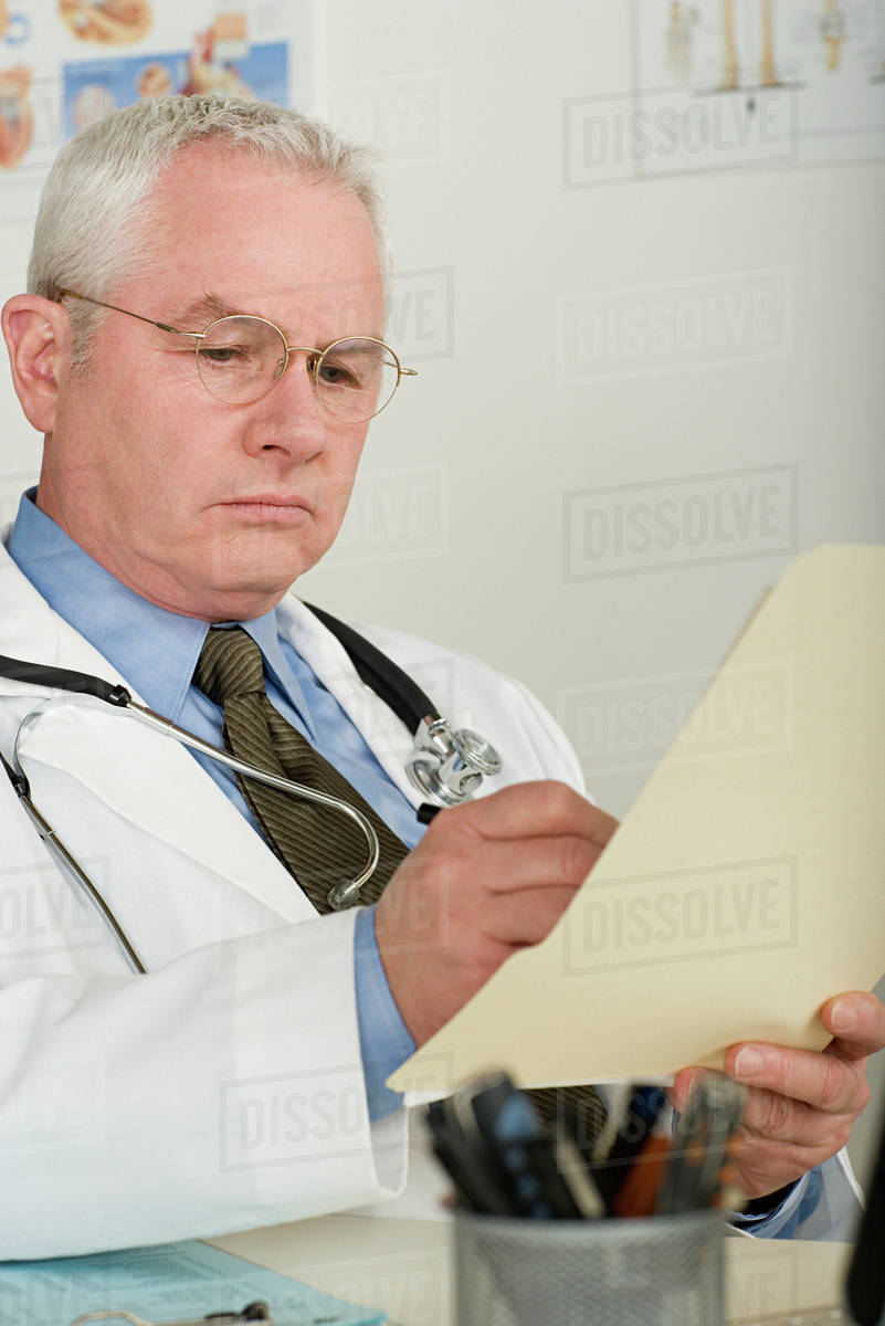 Doctor reading medical document - Stock Photo - Dissolve