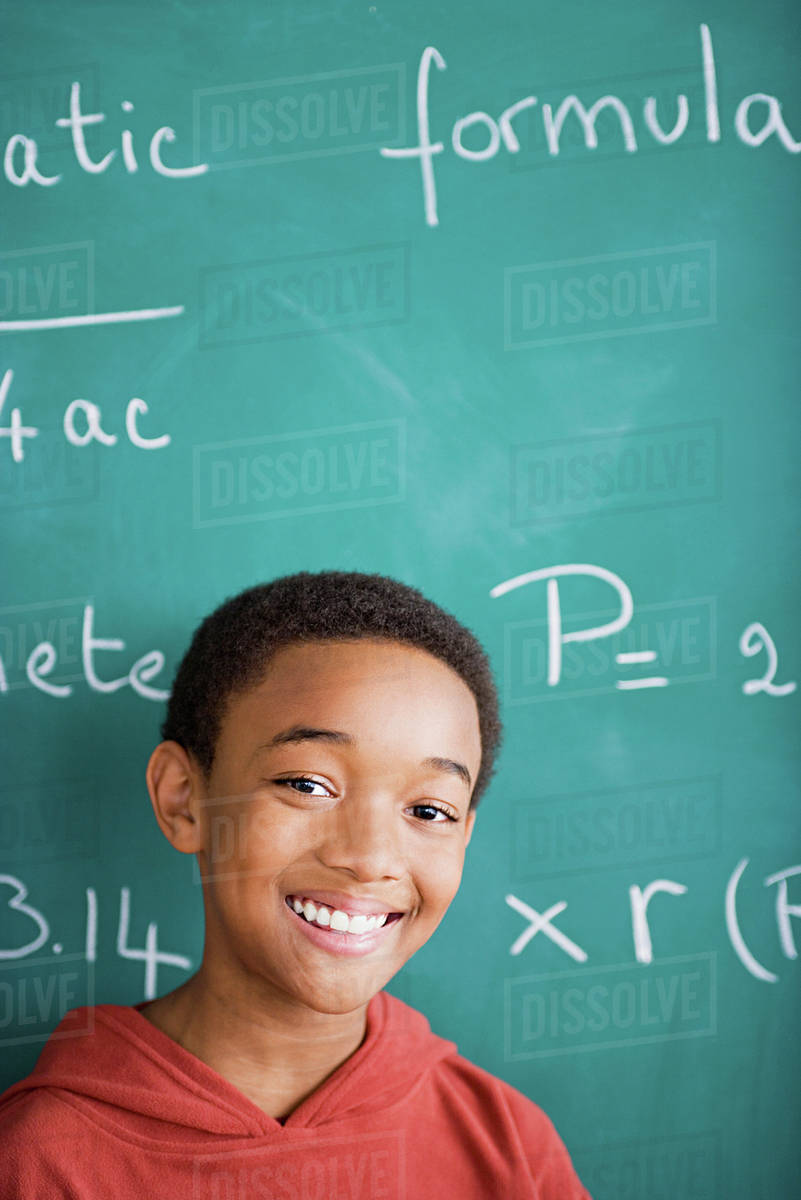Happy young boy standing against blackboard after solving mathematical ...