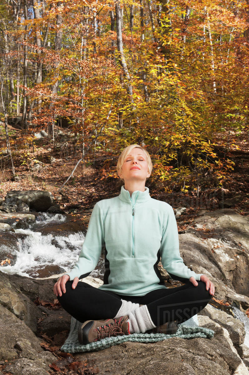 Woman meditating by stream in forest - Stock Photo - Dissolve