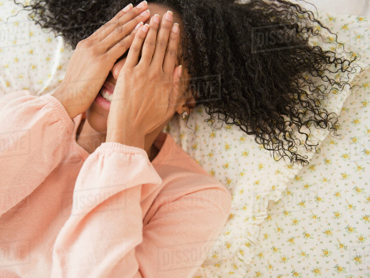 Woman lying down on bed, covering face with her hands - Royalty-free ...