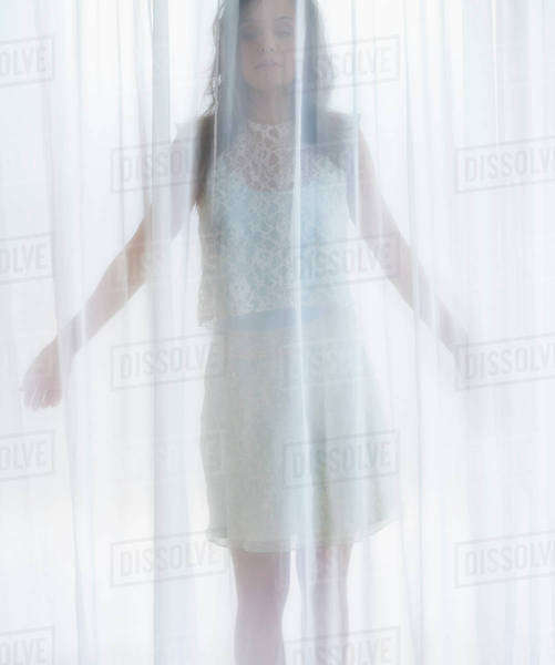 Portrait of young woman behind curtain - Stock Photo - Dissolve