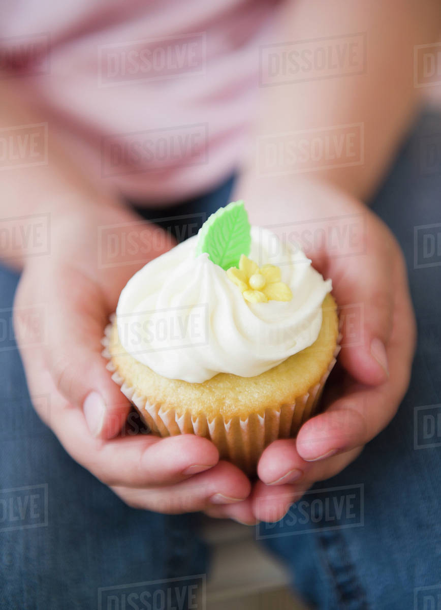 Close up of girl's (8-9) hands holding cupcake - Stock Photo - Dissolve