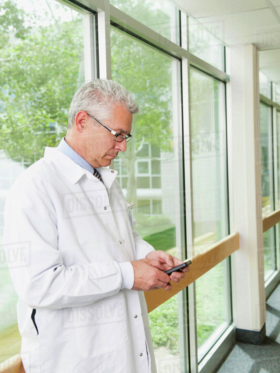 Doctor using mobile phone while standing in hospital corridor - Royalty ...