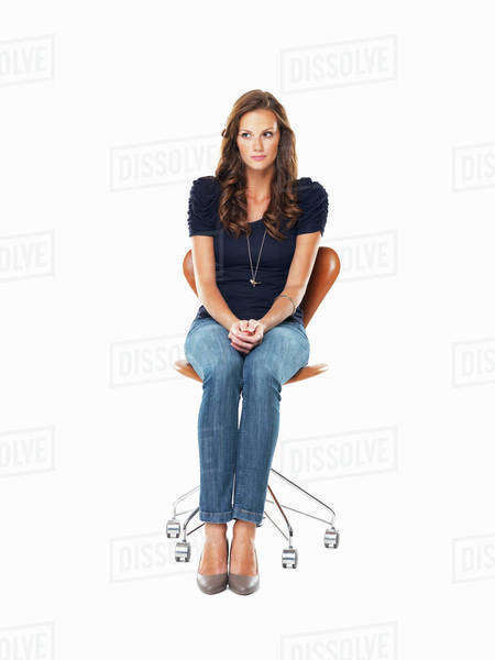 Studio shot of young woman sitting on chair with hands clasped ...