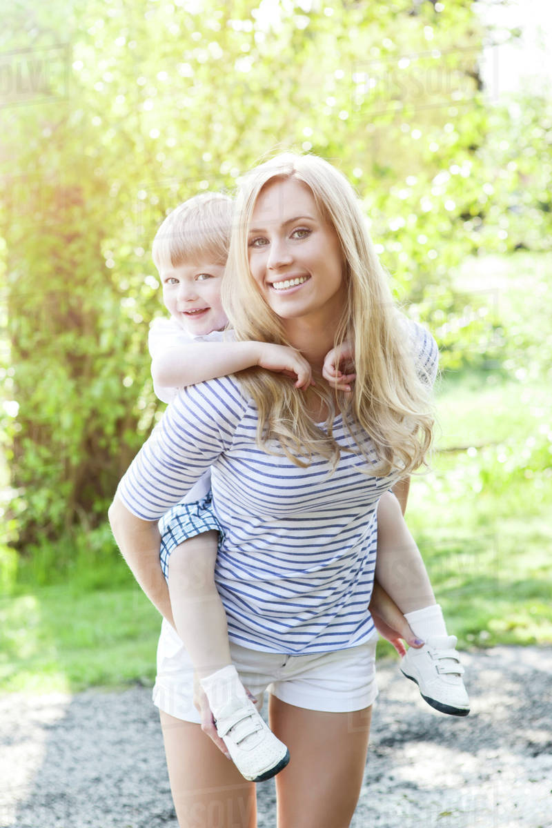 Young woman giving piggyback ride to son (2-3) in park - Stock Photo ...