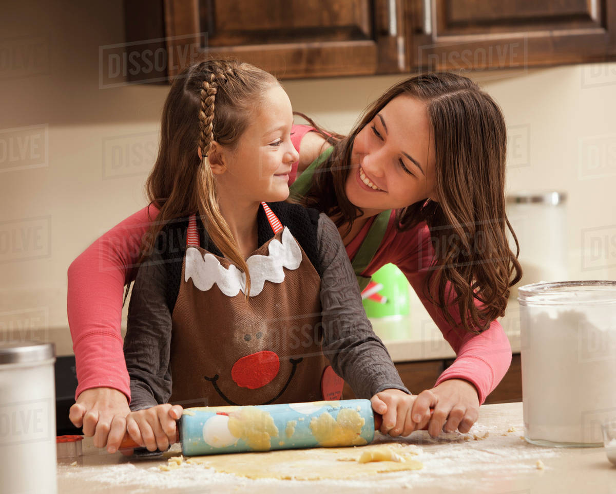 Two sisters (6-7, 18-19) rolling dough - Stock Photo - Dissolve