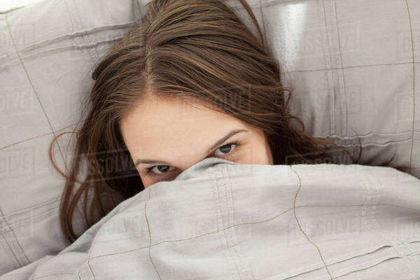 Portrait of young woman lying in bed hiding under bedding - Stock Photo ...