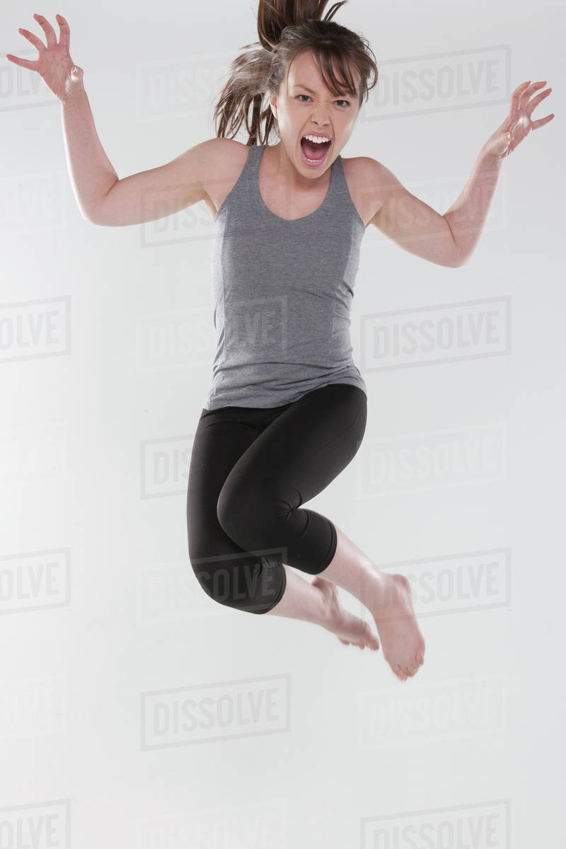Portrait of young woman jumping, studio shot - Stock Photo - Dissolve