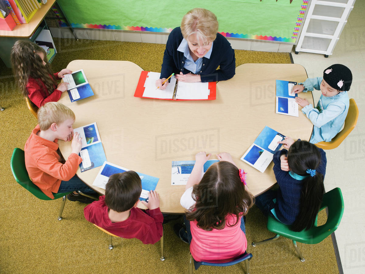Kindergarten students sitting at table with their teacher - Royalty ...