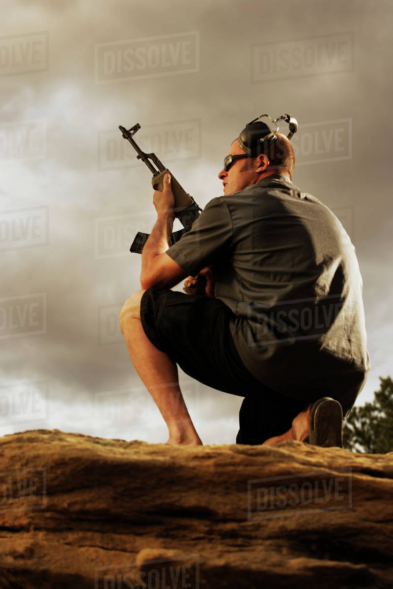 Man holding gun on rocks - Royalty-free Stock Photo | Dissolve