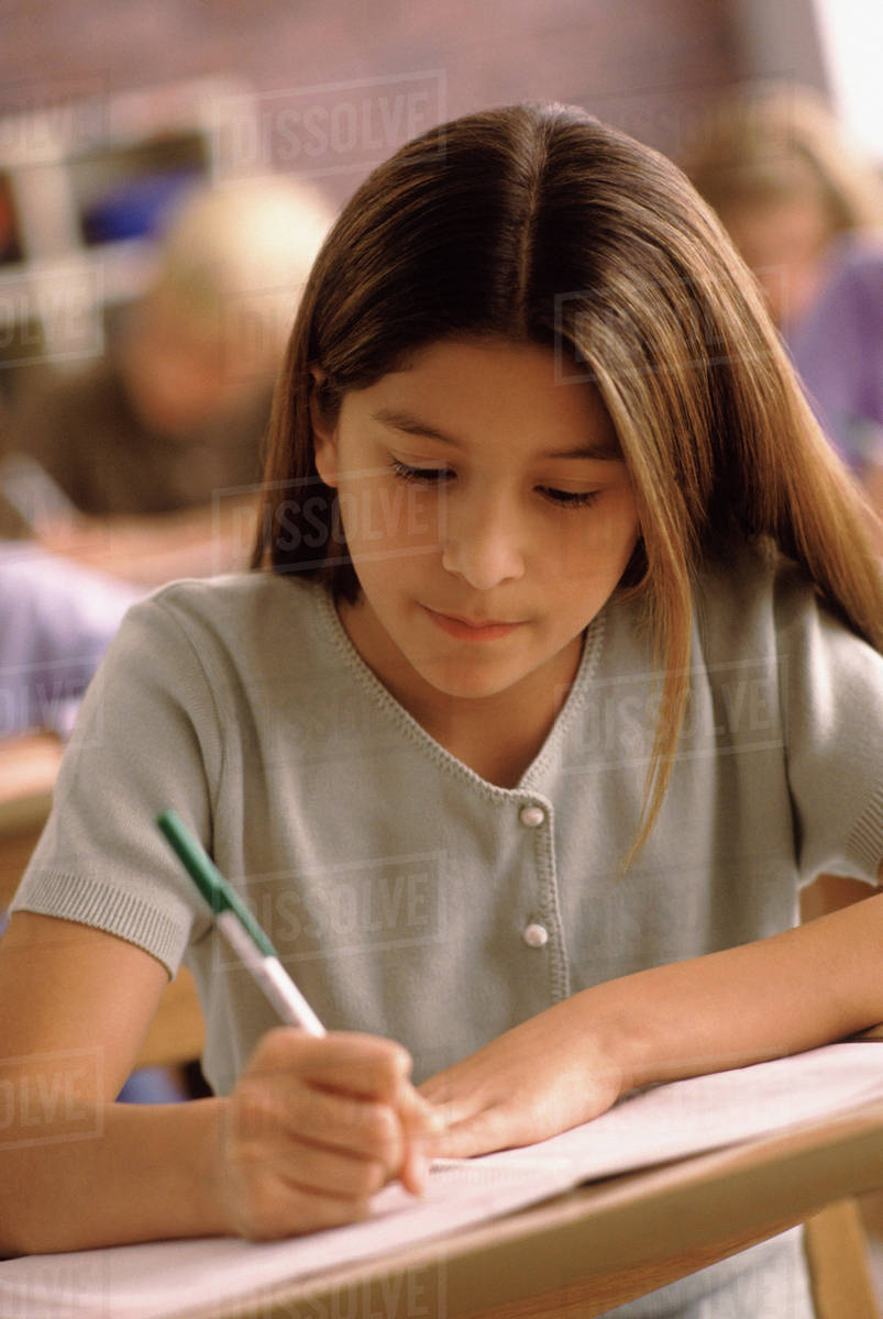Elementary school student writing at her desk - Stock Photo - Dissolve