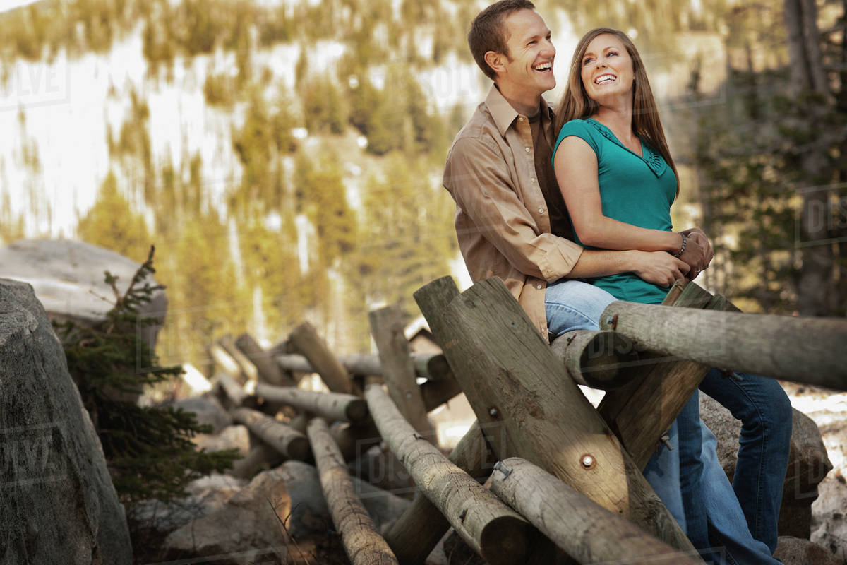 Laughing couple sitting on log fence - Royalty-free Stock Photo | Dissolve