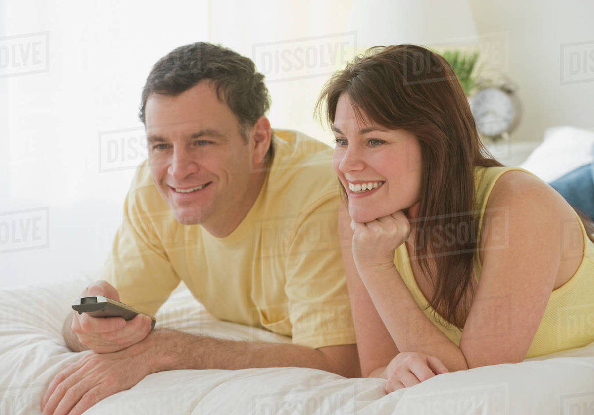 Couple pointing remote control on bed - Stock Photo - Dissolve