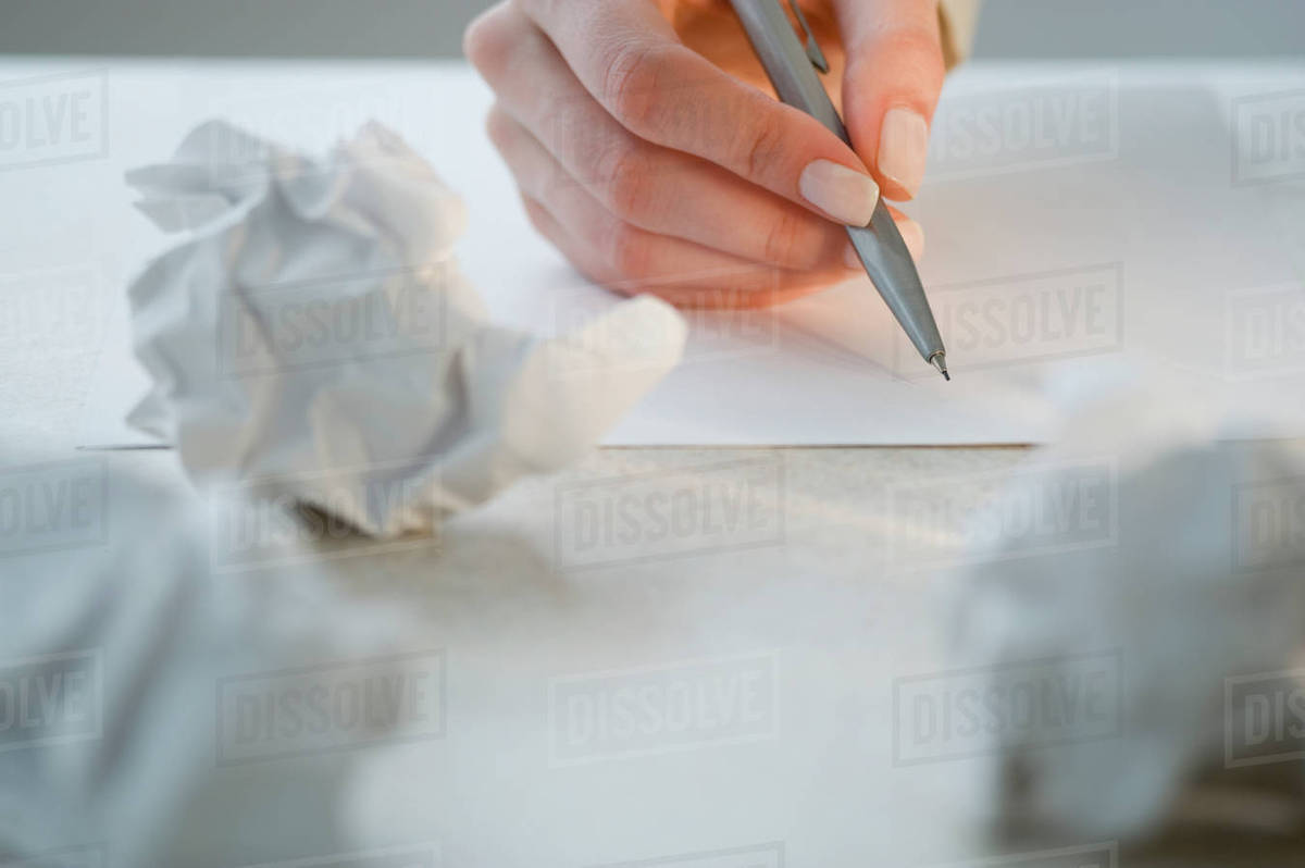 Woman writing next to crumpled papers - Stock Photo - Dissolve