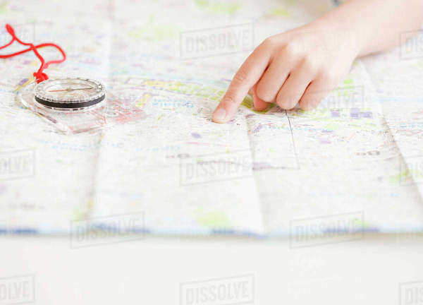 Child pointing at map next to compass - Royalty-free Stock Photo | Dissolve
