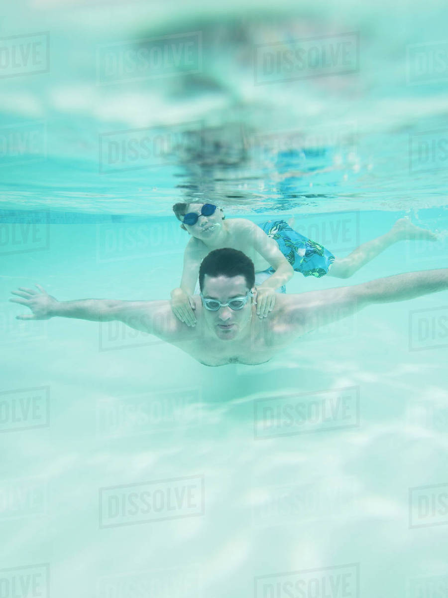 Boy swimming on father’s back underwater - Stock Photo - Dissolve