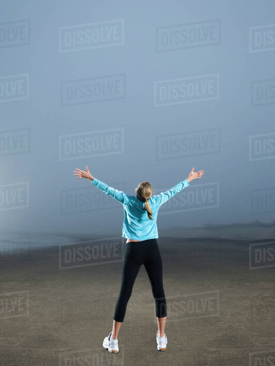 Woman with arms outstretched on foggy beach - Stock Photo - Dissolve