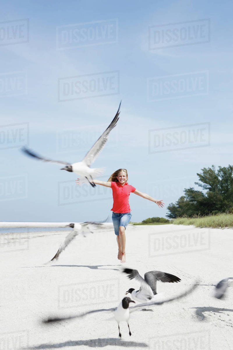 Girl chasing birds on beach - Royalty-free Stock Photo | Dissolve