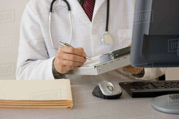 Doctor writing on chart at desk - Royalty-free Stock Photo | Dissolve
