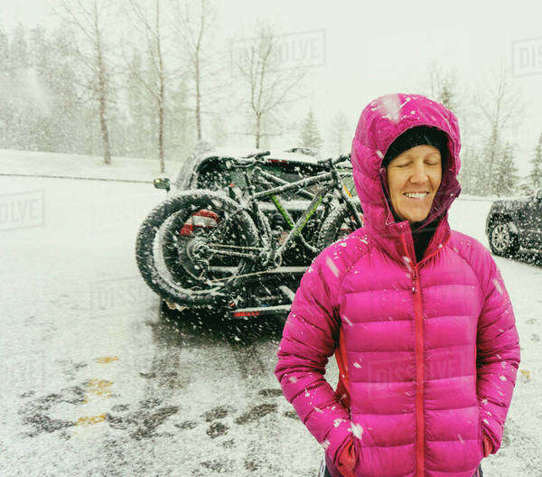 Smiling woman stands beside a car loaded with bikes in a snowstorm ...