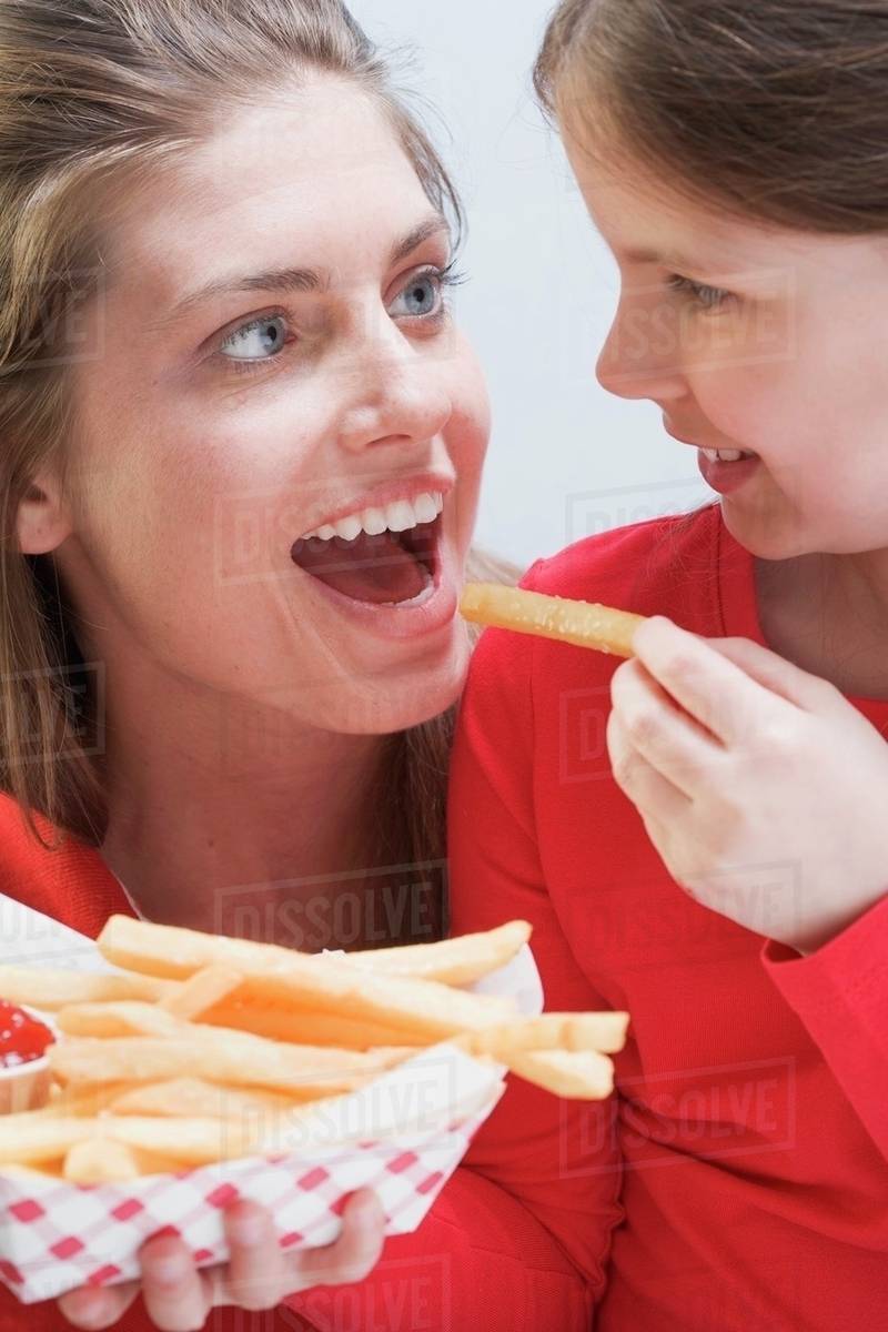 Young woman and girl eating chips together - Stock Photo - Dissolve