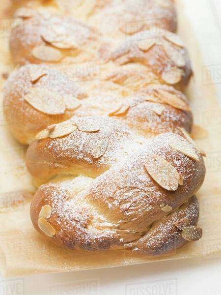 Bread plait with flaked almonds & icing sugar on baking parchment ...