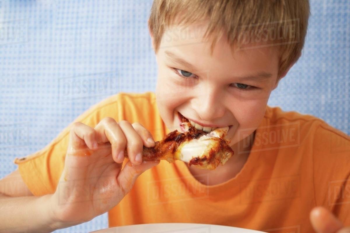 Young boy biting into a chicken drunstick - Stock Photo - Dissolve