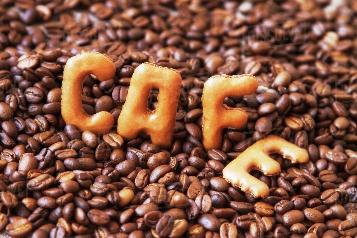 The word 'cafe' written using alphabet biscuits on top of coffee beans ...