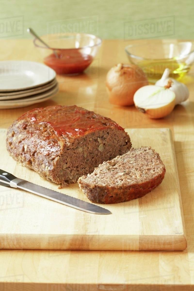 Partially Sliced Meatloaf on Cutting Board; Plates and Ingredients ...