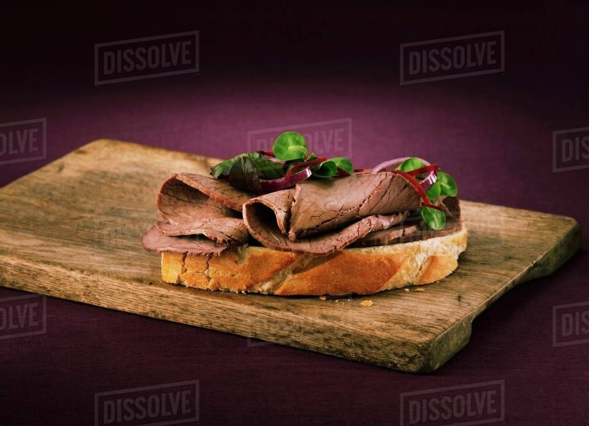 A slice of white bread topped with roast beef on a wooden board - Stock ...