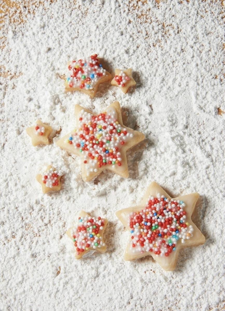 Star biscuits with coloured sprinkles on a sugared wooden board ...