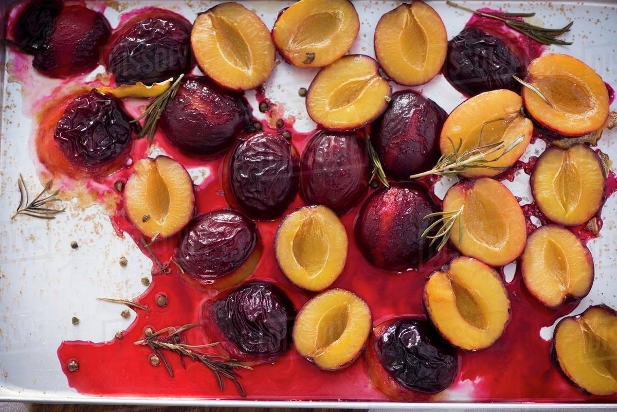 Oven roasted damsons with rosemary on a baking tray (seen from above ...