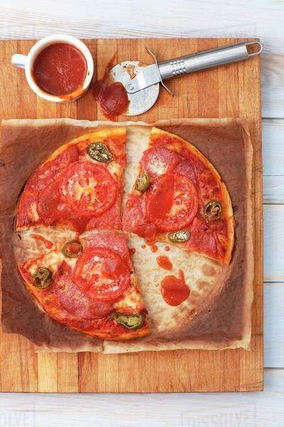 A pizza with salami and jalapenos, sliced - Stock Photo - Dissolve