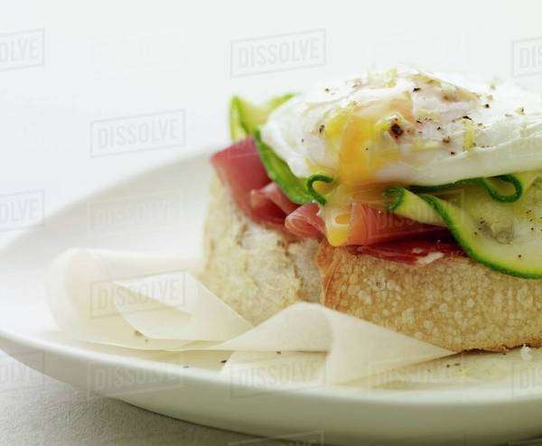Toasted bread with ham and courgette, topped with a poached egg - Stock ...