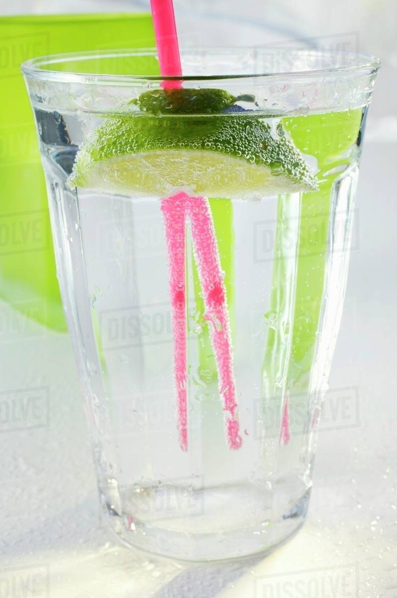 Glass of water with wedge of lime and straw - Stock Photo - Dissolve