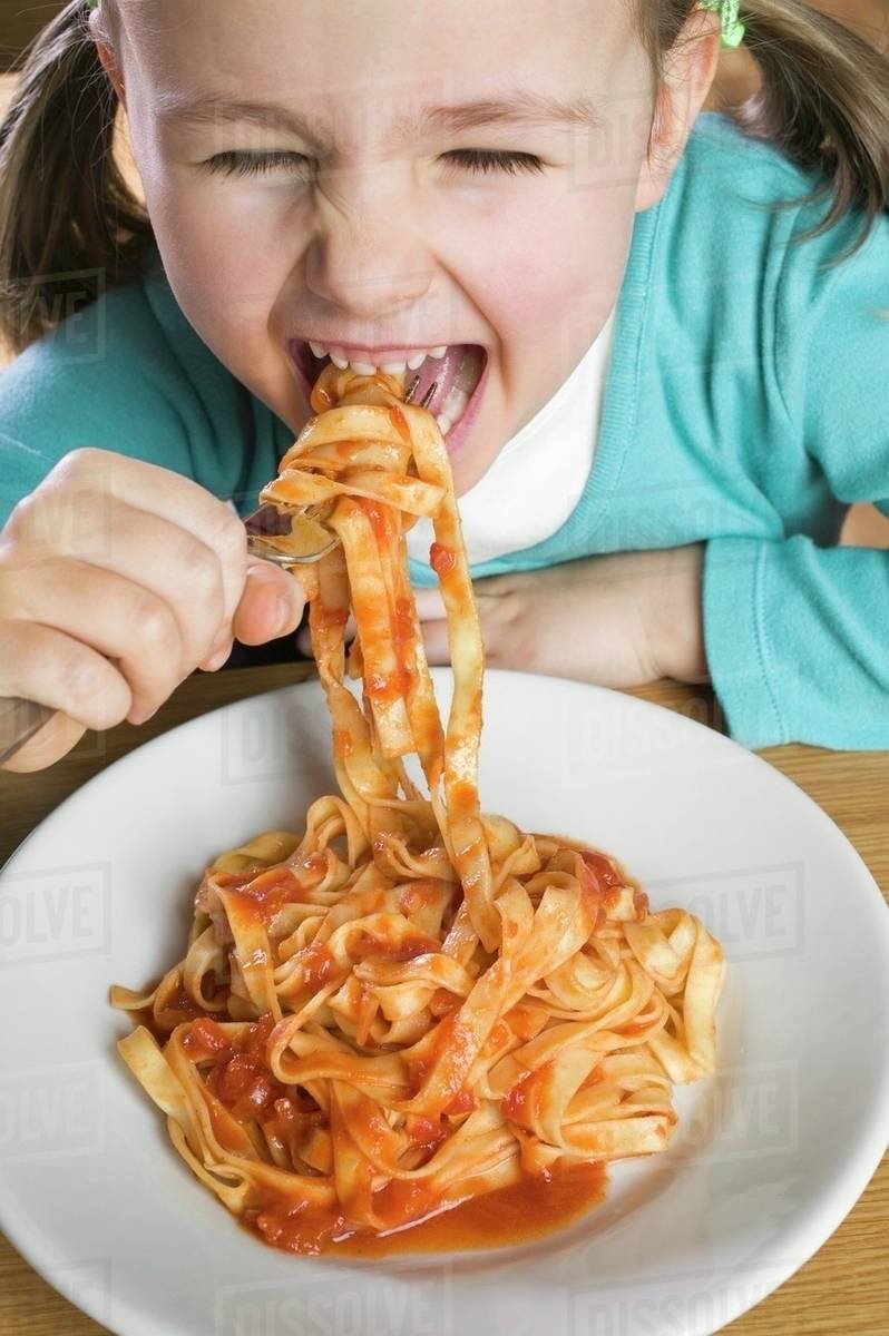 Small girl eating ribbon pasta with tomato sauce - Stock Photo - Dissolve