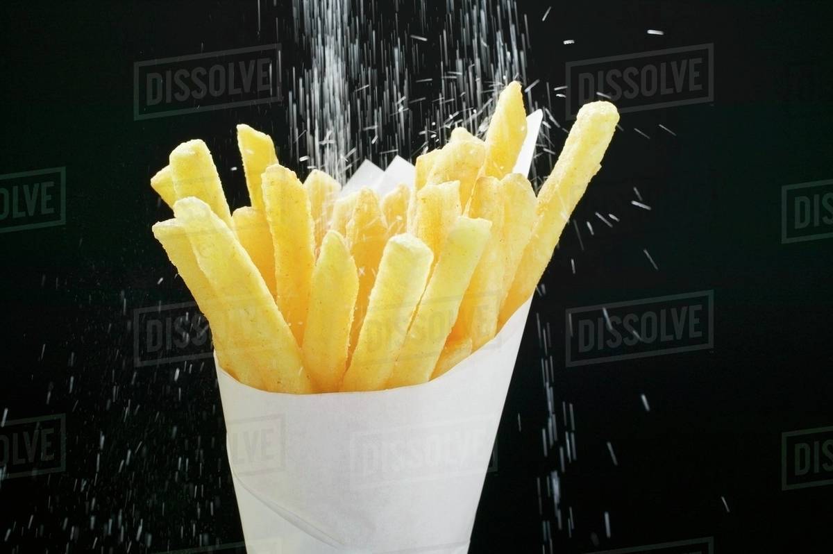 Sprinkling salt on chips in paper cone - Royalty-free Stock Photo ...