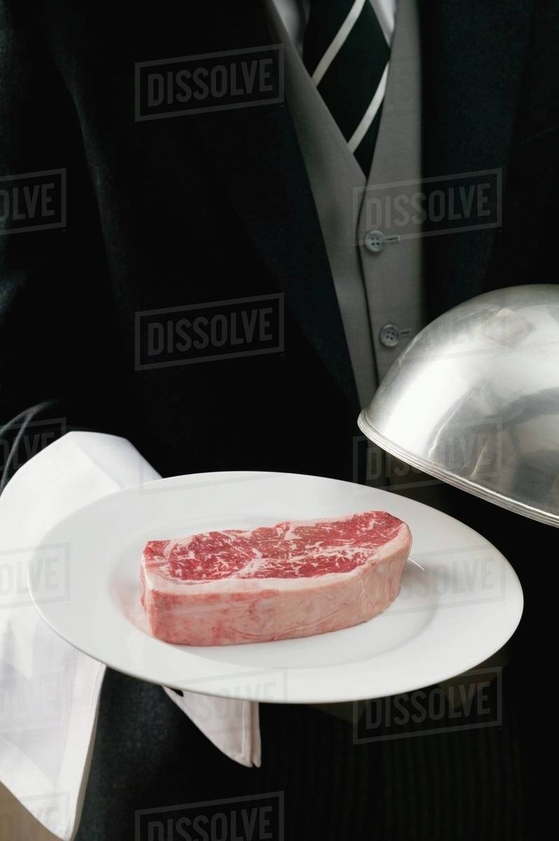 Butler serving raw beef steak on plate with dome cover - Royalty-free ...