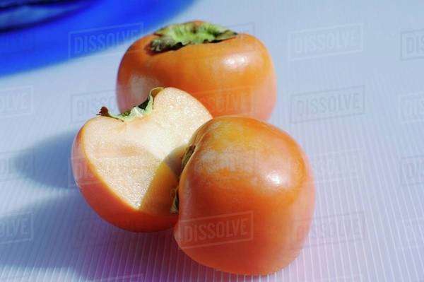 One whole and one halved sharon fruit - Stock Photo - Dissolve