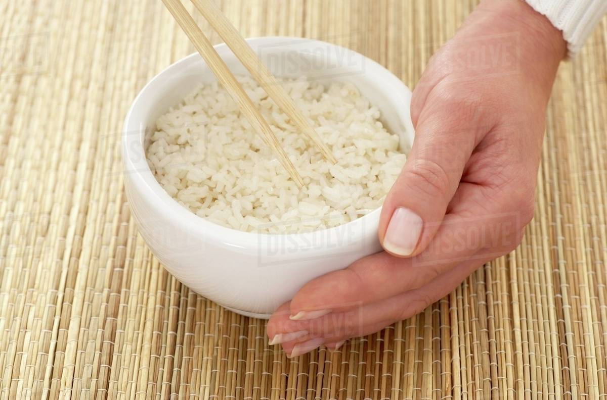 Woman's hand holding a bowl of rice firmly on a bast cover - Stock ...