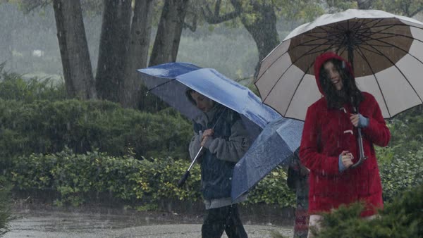 Kids in the pouring rain having fun jumping with umbrellas - slow ...