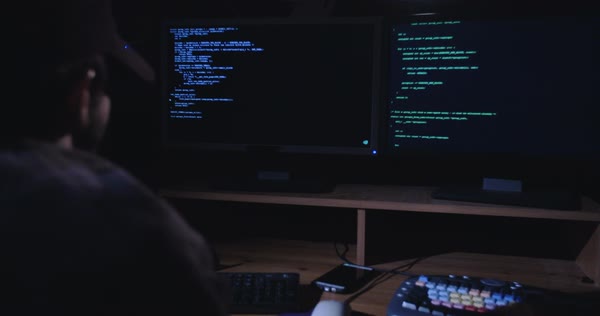 Computer Hacker sitting in a dark room in front of screens and writing ...