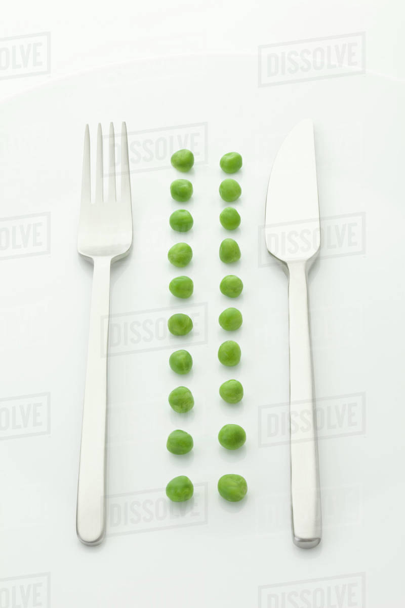 Row of green peas with fork and knife - Stock Photo - Dissolve