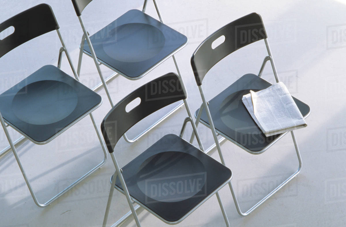 Newspaper on one of four fold up chairs - Stock Photo - Dissolve