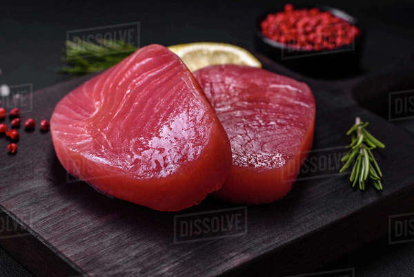 Two fresh slices of raw tuna fillet with spices and herbs on a dark ...