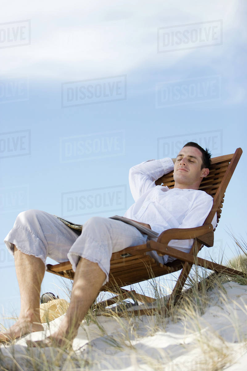Young man lounging in deckchair, eyes closed - Royalty-free Stock Photo ...