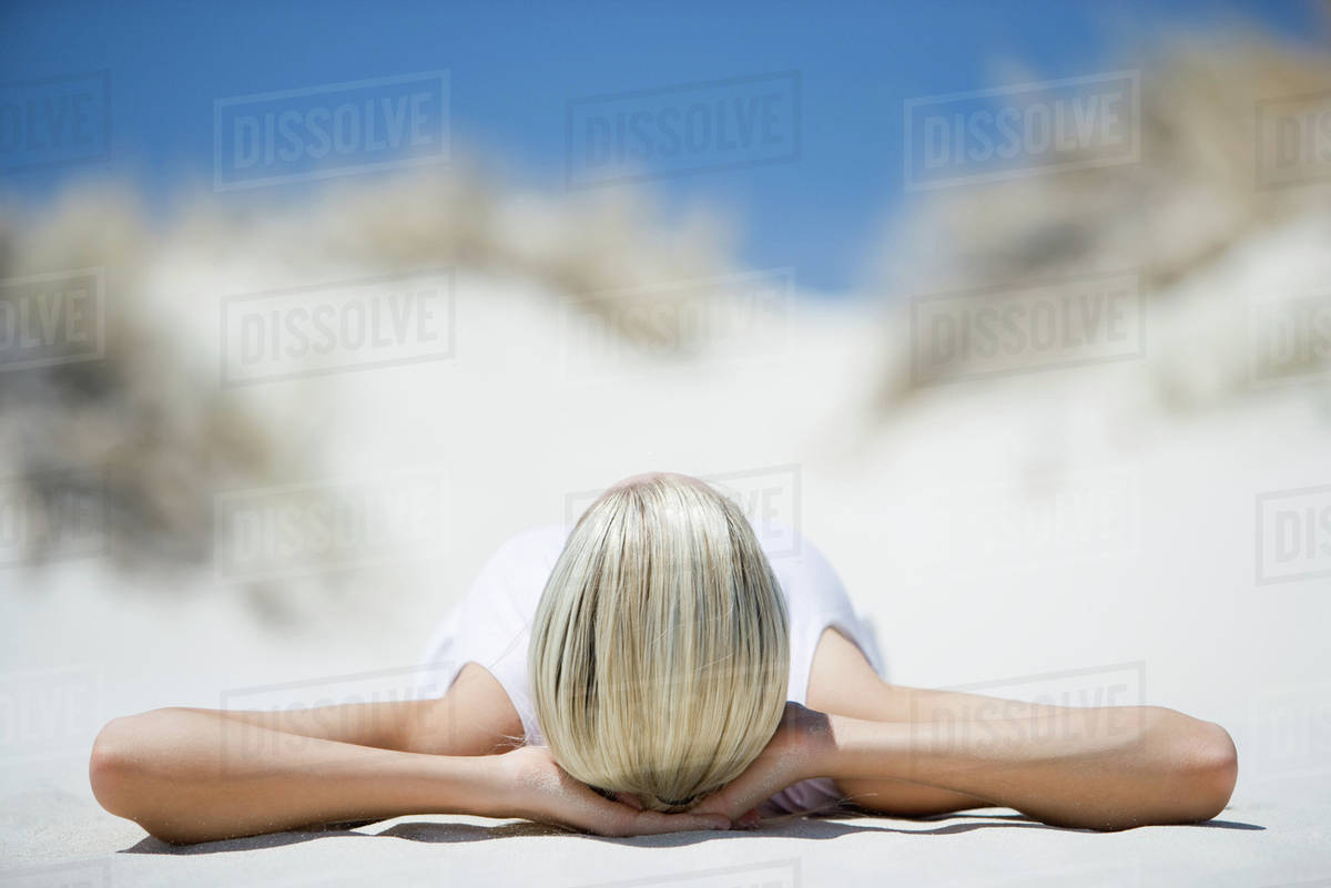 Young woman lying on beach, surface level, view of hands under head ...
