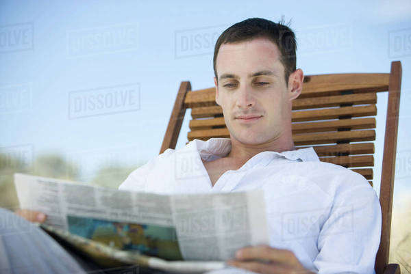 Young man reading newspaper in deckchair - Stock Photo - Dissolve