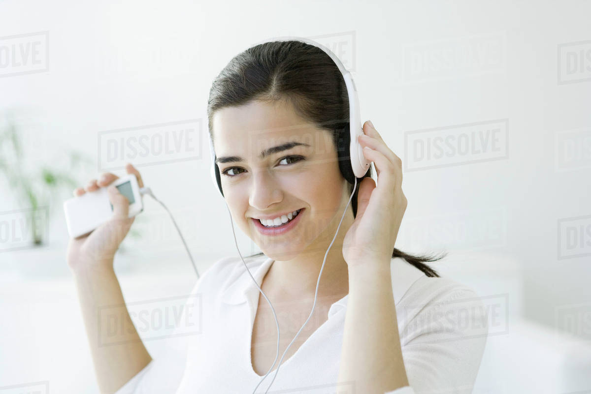 Woman listening to MP3 player with headphones, smiling at camera ...